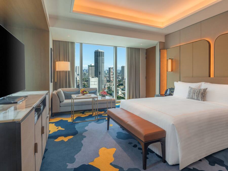 Quarto de hotel moderno com uma cama grande, uma escrivaninha, uma cadeira e vista para a cidade.