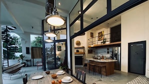 Cozinha moderna com ilha grande, eletrodomésticos de aço inoxidável e área de jantar com mesa de madeira comprida posta para seis pessoas.