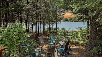 Área externa à beira do lago com cadeiras Adirondack e uma lareira.