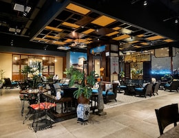 Um restaurante com interior moderno, com móveis de madeira e metal, chão de azulejos e teto com padrão geométrico.