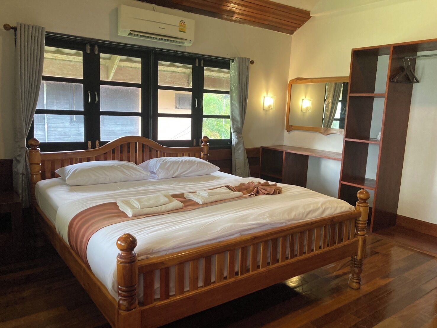 Uma cama de madeira com cabeceira, mesa de cabeceira, espelho e guarda-roupa.