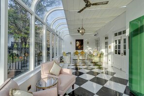 Um quarto amplo com grandes janelas, um chão quadriculado e uma porta verde.