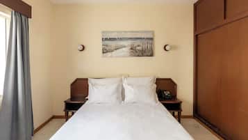 Quarto de hotel com uma cama, uma mesinha de cabeceira, um quadro na parede e um guarda-roupa de madeira.