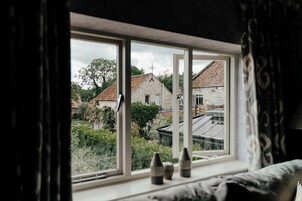 Quarto com uma grande janela com vista para um jardim e edifícios de pedra.
