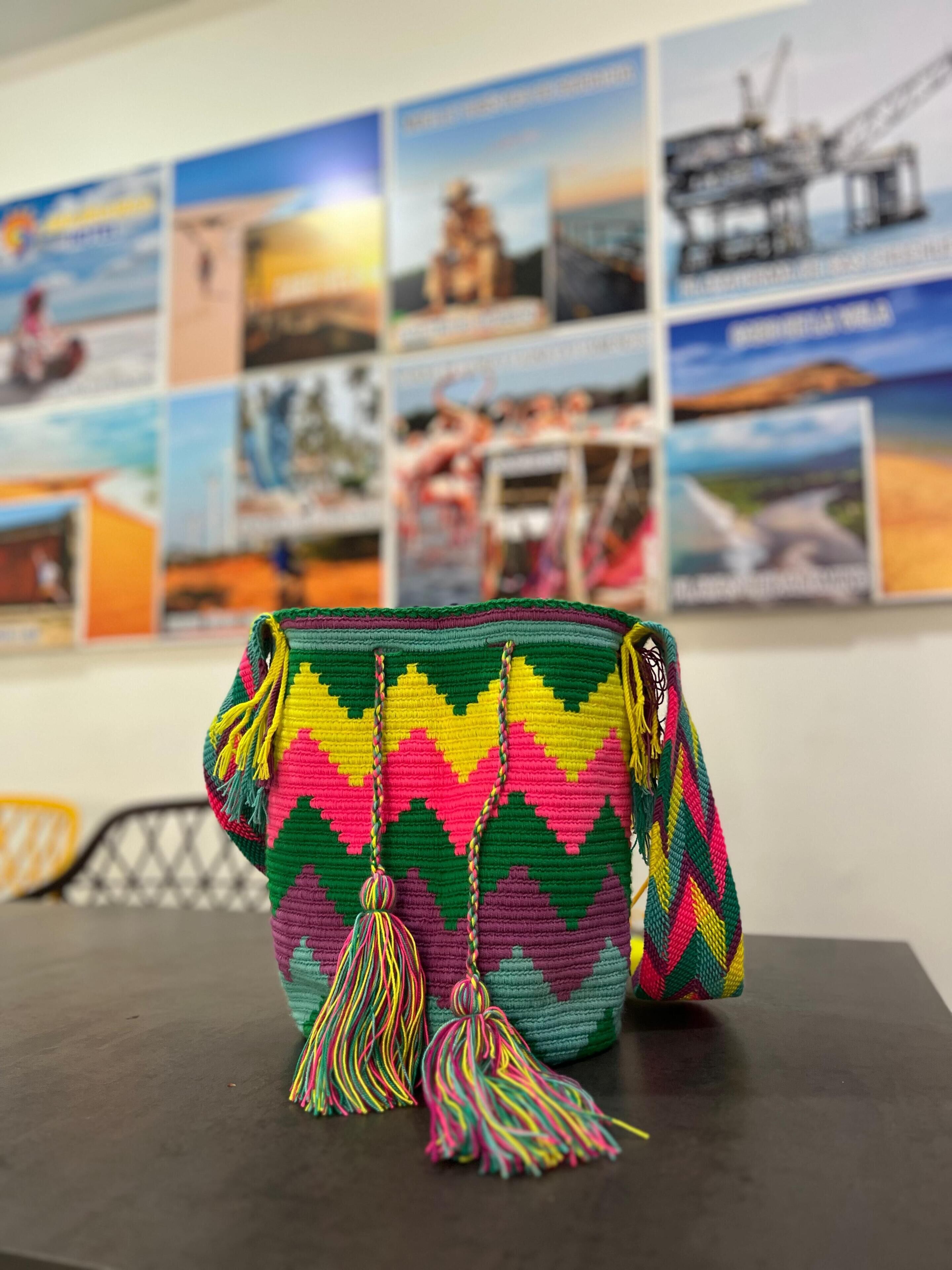 Uma bolsa colorida, tecida e com borlas, sobre uma mesa.