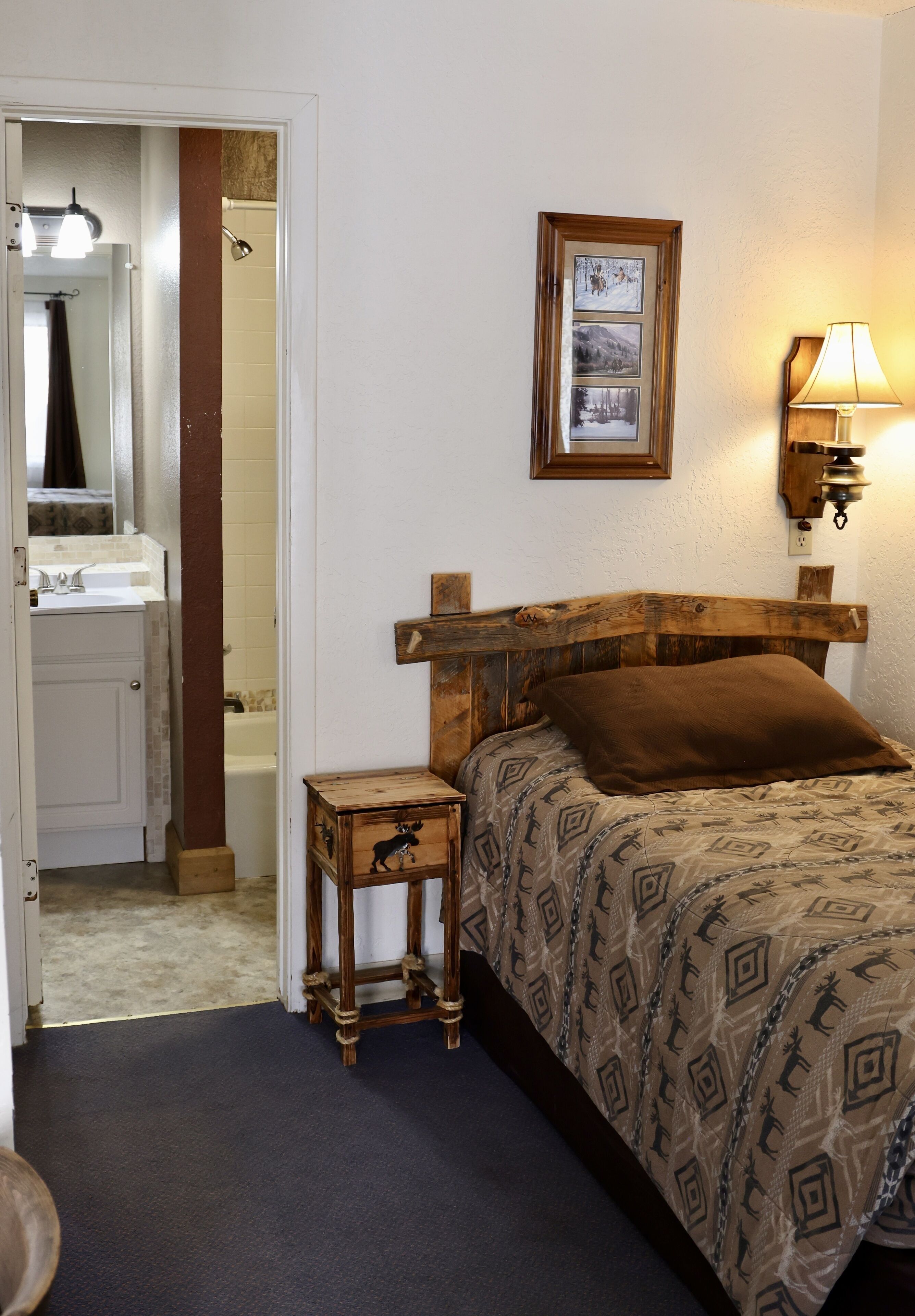 Quarto com cabeceira de madeira, mesa de cabeceira, abajur e quadro pendurado na parede.