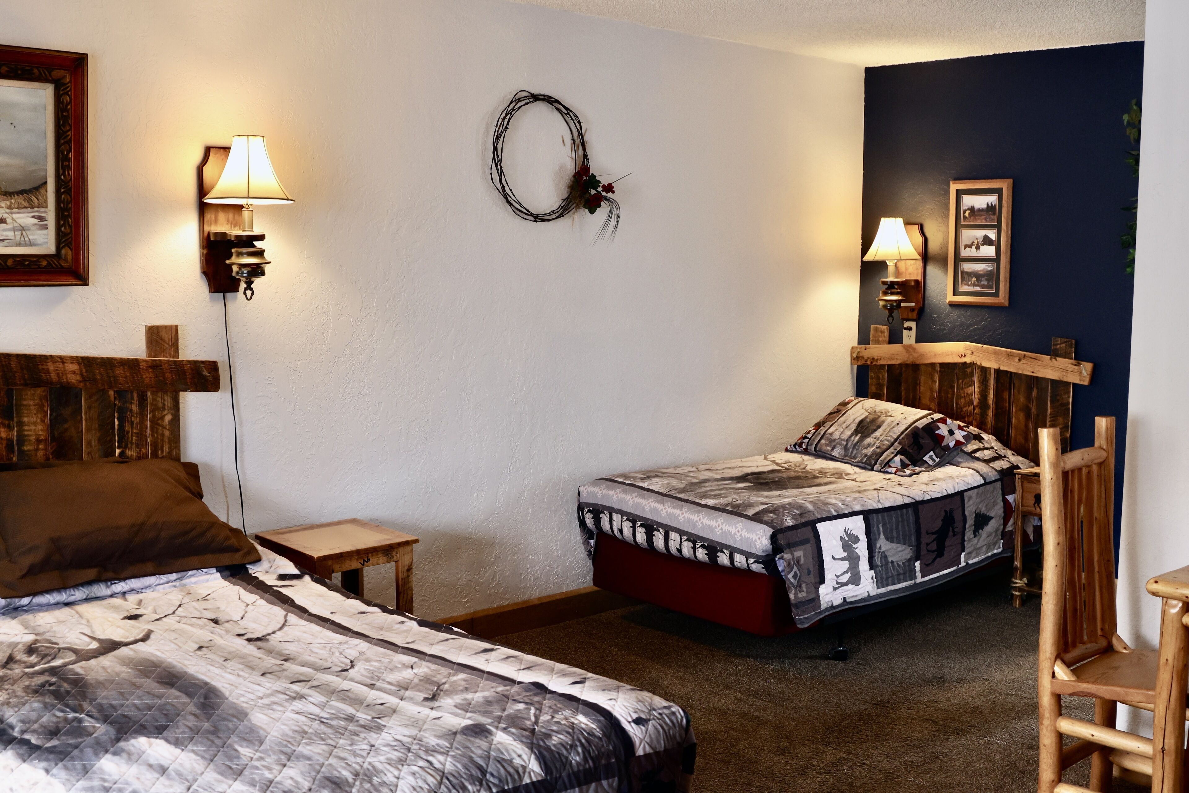 Quarto com duas camas, uma cabeceira de madeira, uma mesinha de madeira e uma luminária na parede.
