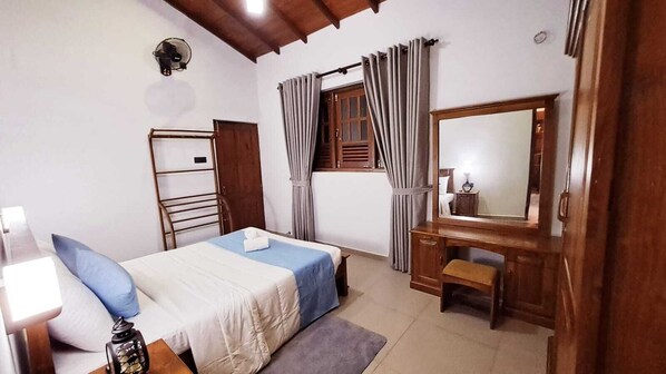 Quarto com cama, escrivaninha de madeira, espelho e janela com cortinas.