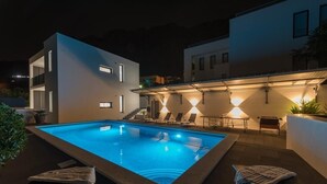 Uma piscina exterior moderna com espreguiçadeiras e uma área de estar coberta.