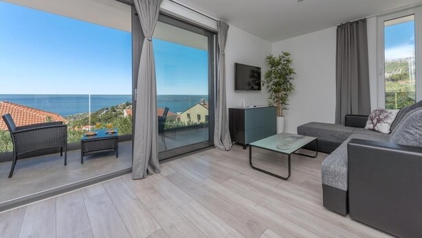 Uma sala de estar moderna com uma grande porta de vidro deslizante que dá para uma varanda com vista para o mar.