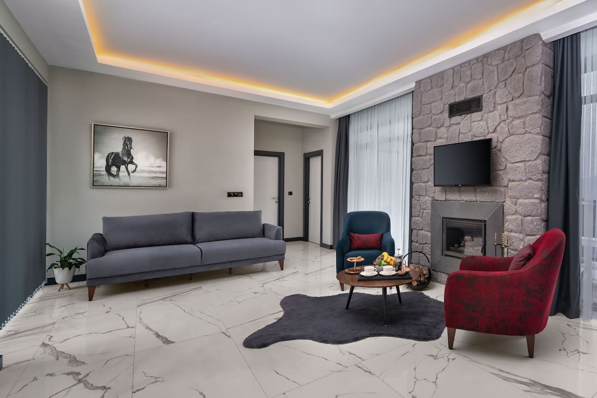 Uma sala de estar moderna com sofá, poltrona, mesa de centro, lareira e um espaço de jantar com mesa posta para dois.