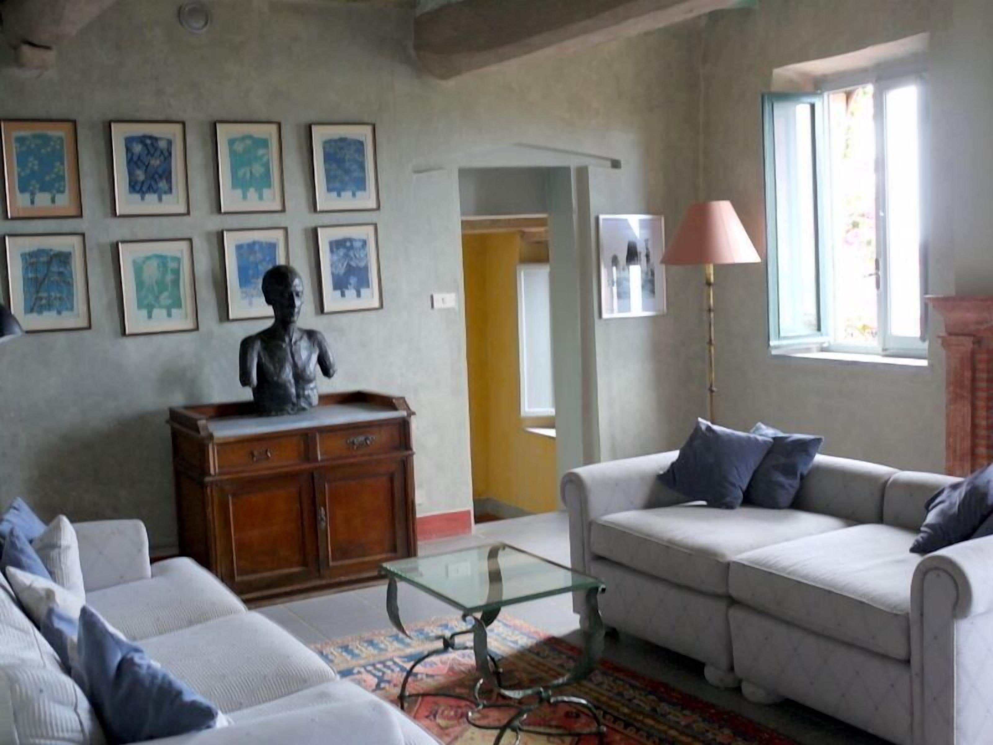 Uma sala de estar com sofá, mesa de centro de vidro, armário de madeira e busto.