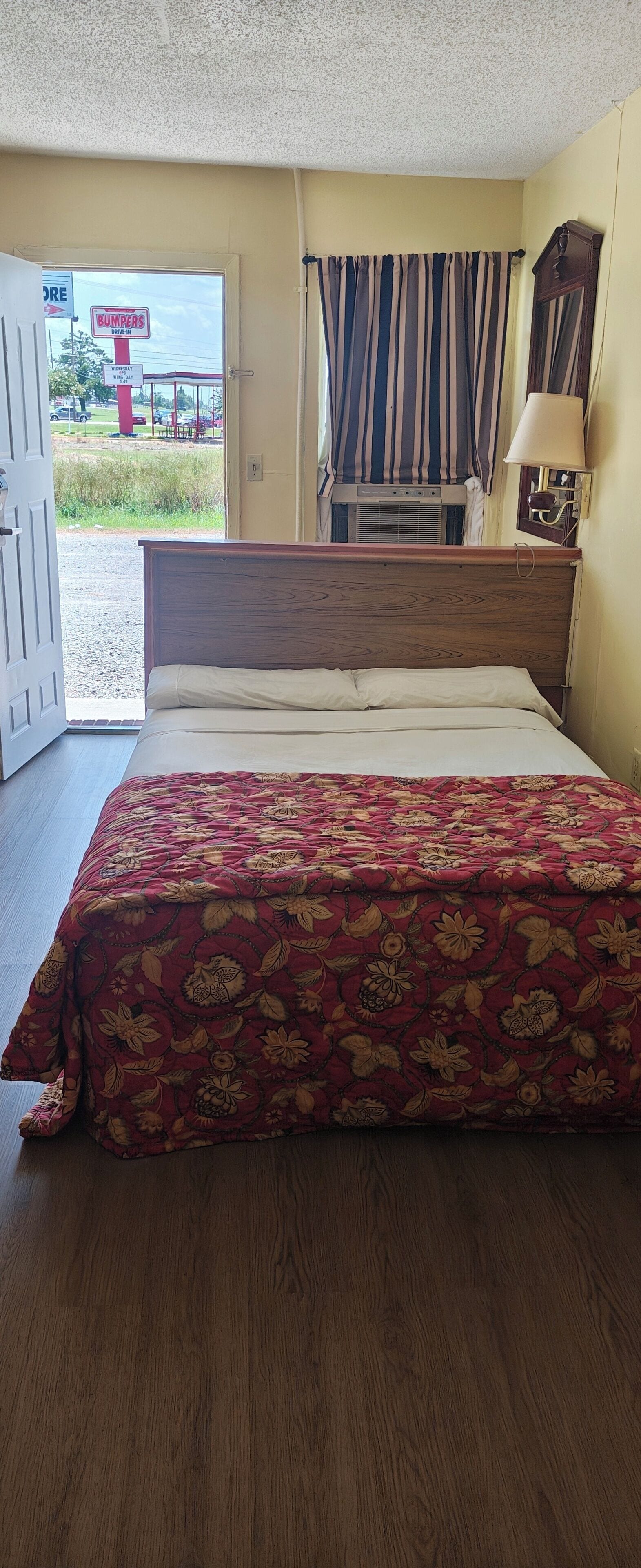 Quarto de hotel com cama, janela com cortinas, abajur e vista para o exterior.