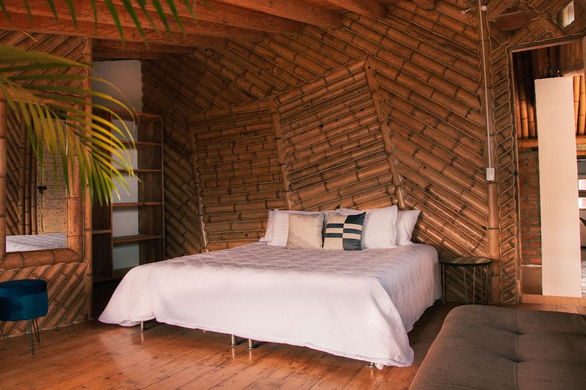 Quarto com cama, uma cadeira e parede de madeira com padrão em espinha de peixe.