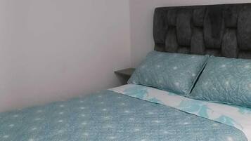 Quarto com cama, cabeceira e mesa de cabeceira.