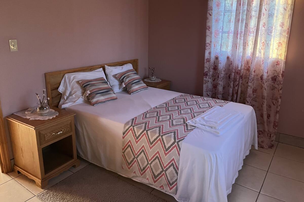 Quarto com cama, mesas de cabeceira, luminária e janela com cortinas.