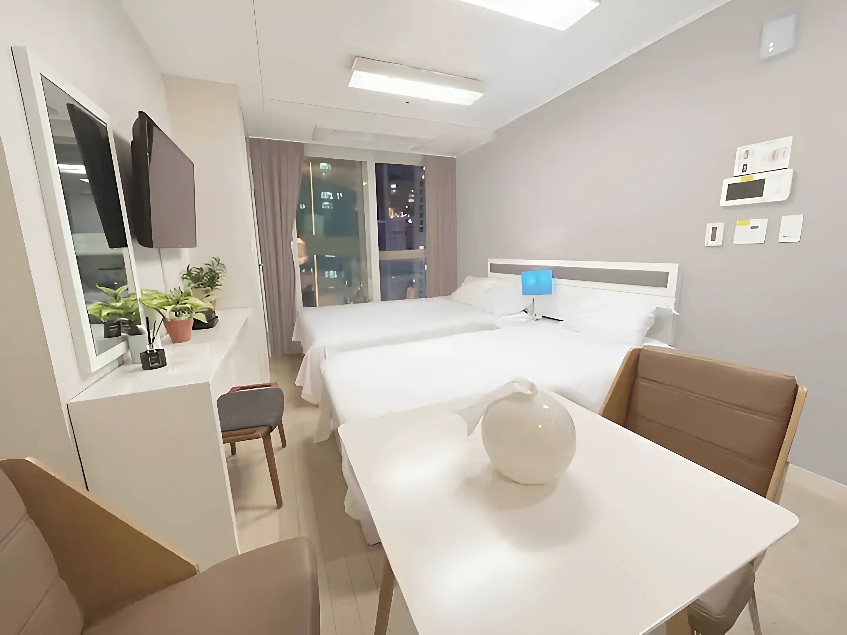Quarto de hotel com duas camas, uma escrivaninha, uma cadeira, uma mesa e uma janela com cortinas.