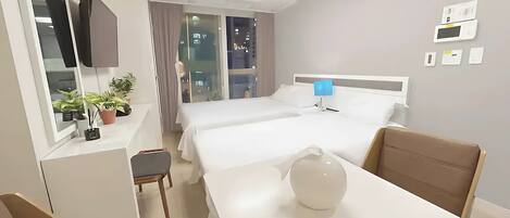 Quarto de hotel com duas camas, uma escrivaninha, uma cadeira, uma mesa e uma janela com cortinas.