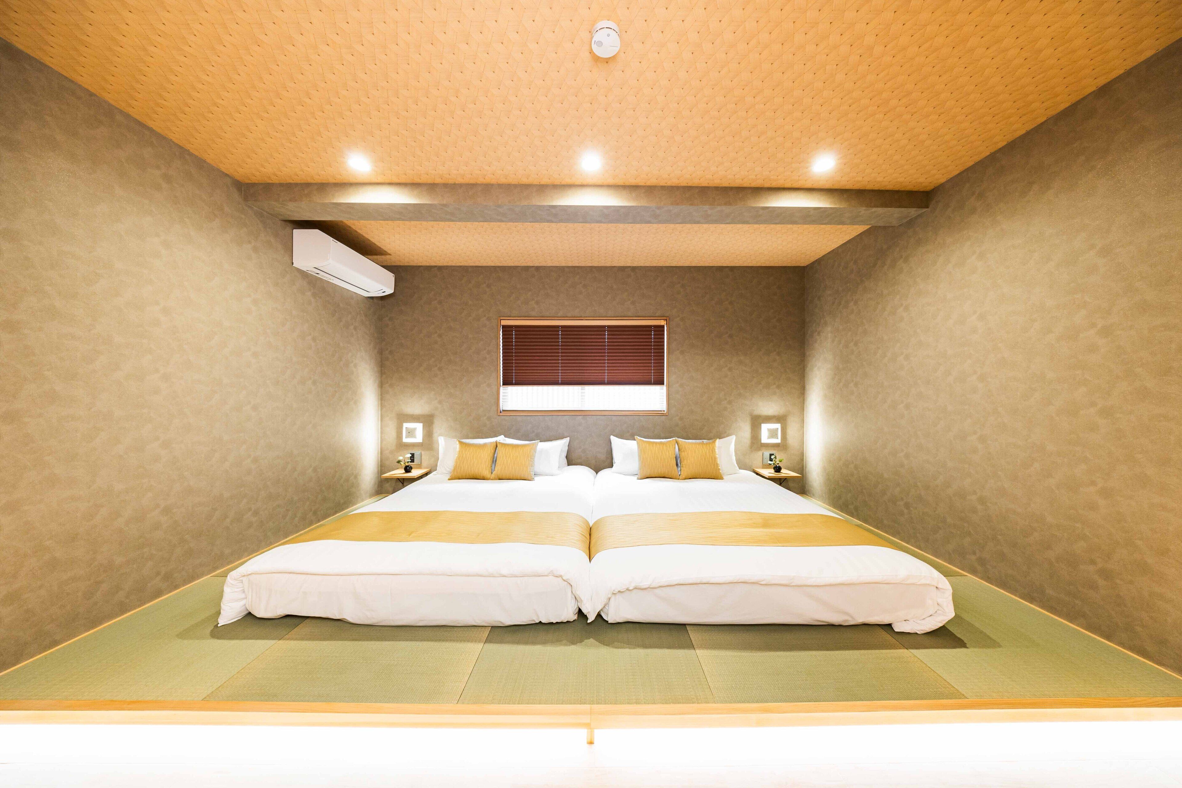 Uma cama de casal com cabeceira de madeira, uma janela pequena com persianas e um ar condicionado fixado na parede.