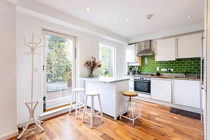 Uma cozinha moderna com armários brancos, um painel verde e piso de madeira.