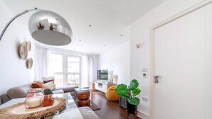 Uma sala de estar moderna com uma mesa de centro de vidro, um sofá, um abajur alto e uma planta em vaso.