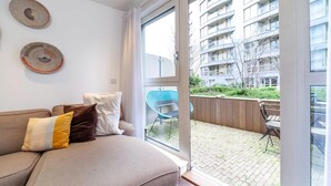 Uma sala de estar moderna com um sofá, duas obras de arte nas paredes e vista para um prédio residencial por uma grande janela.