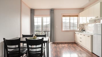Cozinha compacta com área de refeições, incluindo uma mesa com cadeiras, uma janela com cortinas e uma geladeira.