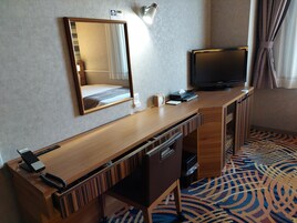Quarto de hotel com escrivaninha de madeira, televisão, espelho e tapete estampado.