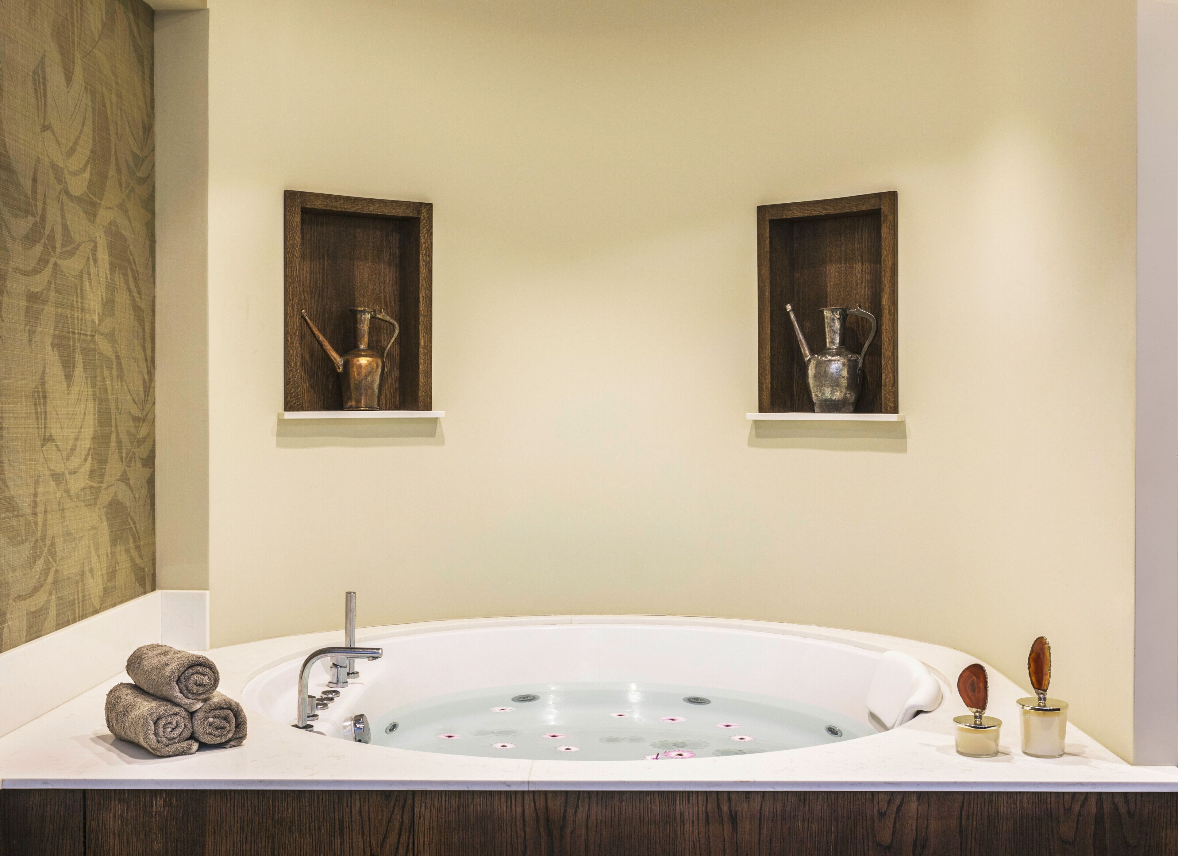 Casa de banho com uma banheira grande, duas pequenas prateleiras com objetos decorativos e um porta-toalhas com toalhas.
