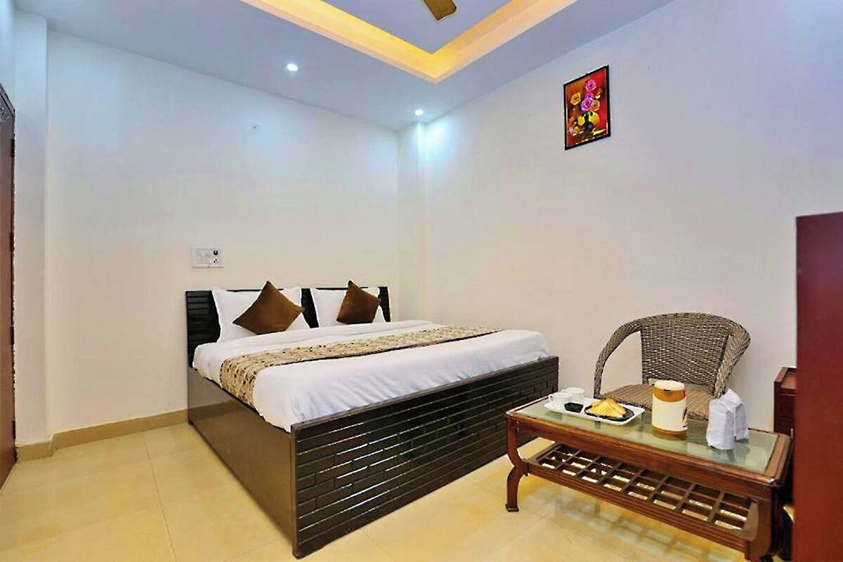 Quarto de hotel com uma cama, uma mesinha com bandeja de comida, uma cadeira de vime e um quadro na parede.