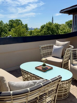 Terraço no telhado com móveis de vime, uma pequena mesa e vista para o horizonte da cidade.