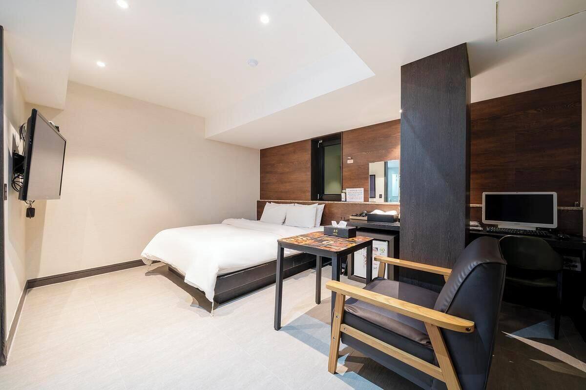 Quarto de hotel moderno com cama, escrivaninha, cadeira, televisão e um espelho grande.