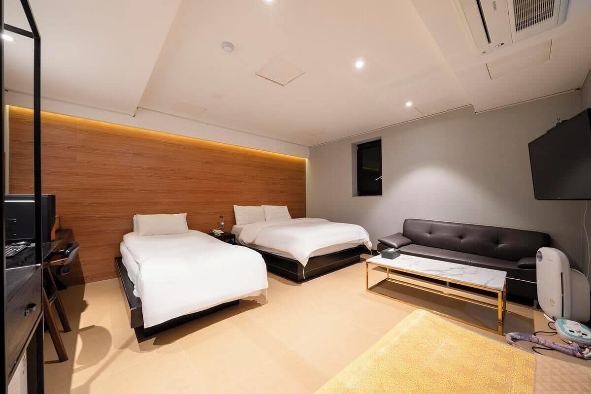 Quarto de hotel moderno com duas camas, televisão de tela plana, sofá e escrivaninha.