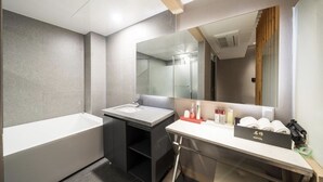 Uma casa de banho moderna com uma banheira, um lavatório e um espelho grande. Há produtos de higiene pessoal no balcão e uma placa com caracteres japoneses.