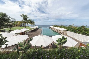Área da piscina com espreguiçadeiras e guarda-sóis, um jardim de cactos e vista para o oceano.
