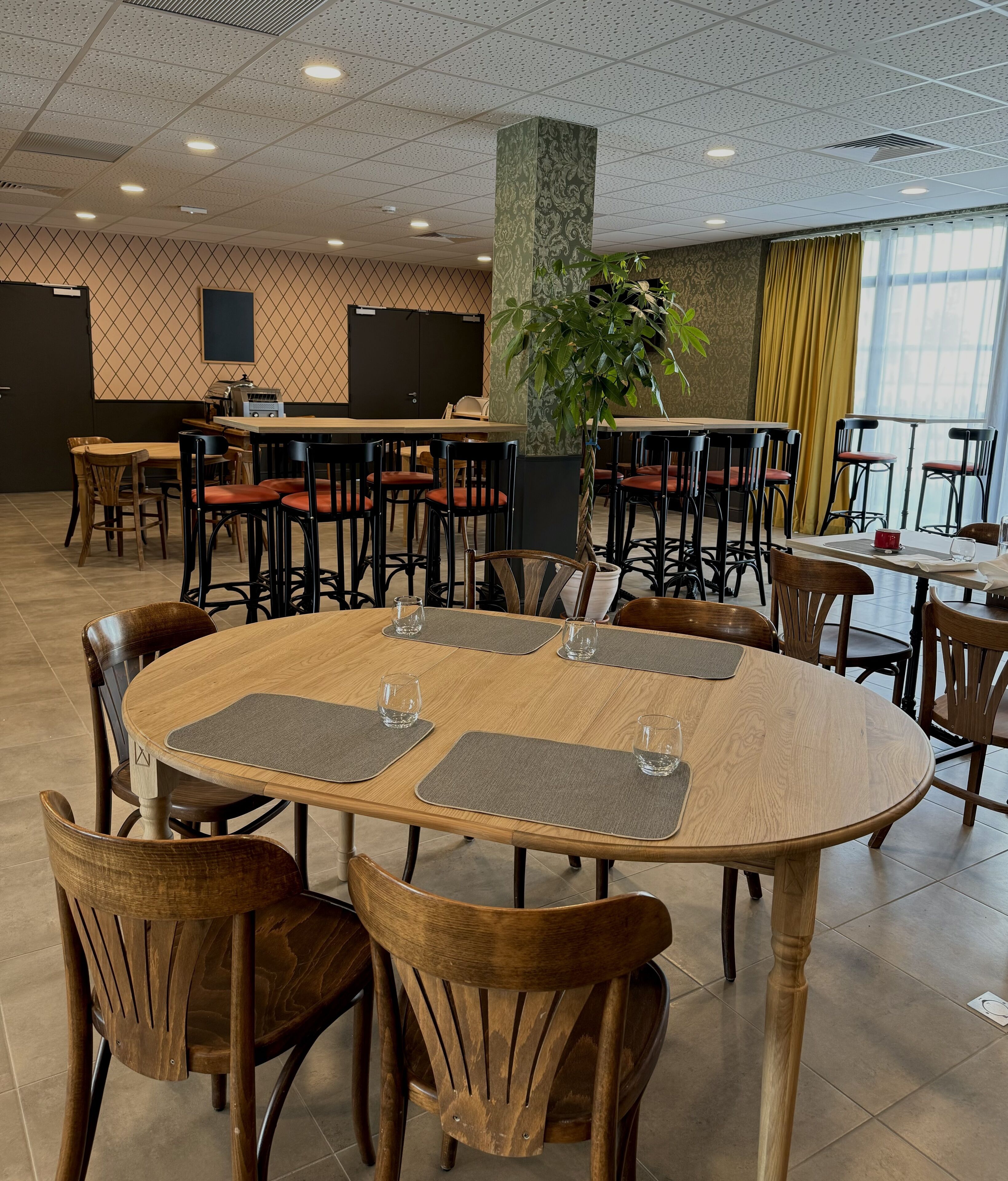 Sala de conferências com uma mesa redonda, cadeiras de madeira e uma grande planta em vaso.