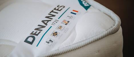 Um close-up de um travesseiro com o texto "DENANTES 1723" e alguns ícones indicando características como "MATTERA PROVAVEL" e "ANTI-BOLSOS".