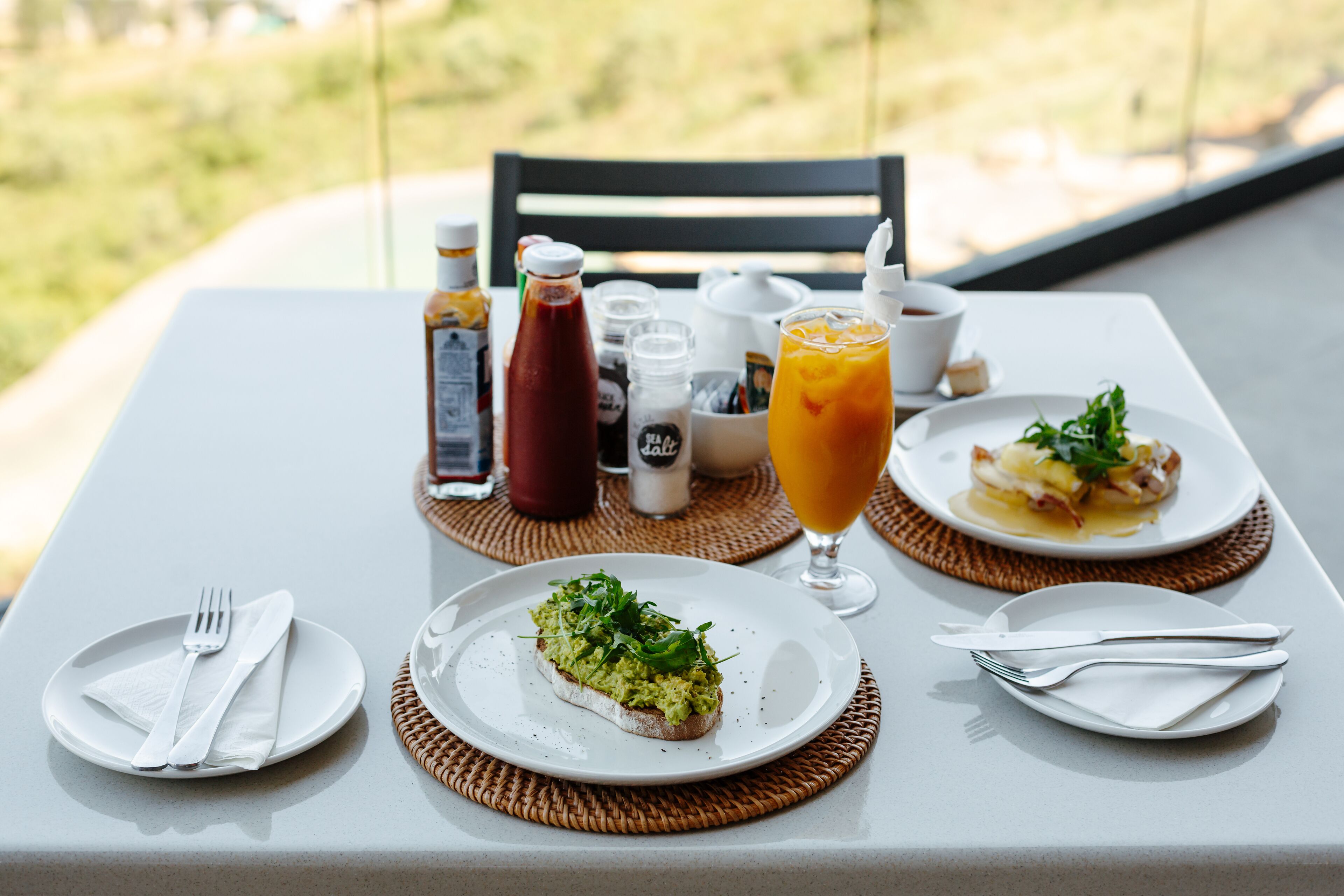 Uma mesa posta com pratos de comida, um copo de suco de laranja e acompanhamentos.