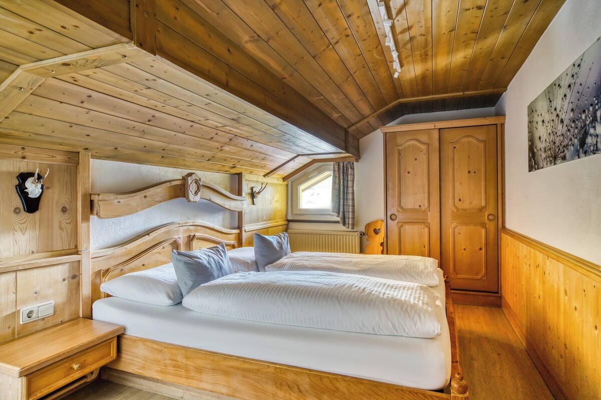 Quarto de madeira com cama grande, cabeceira de madeira e janela com cortinas.