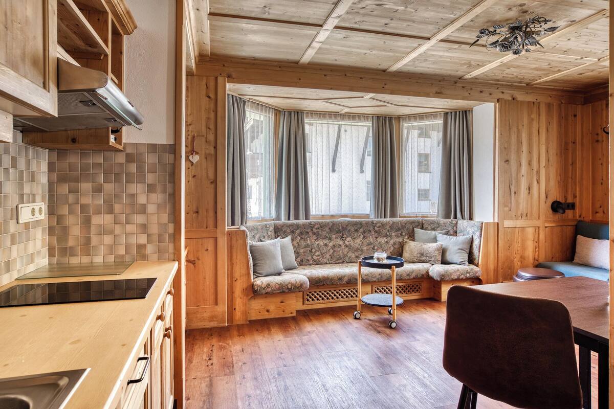 Um quarto acolhedor em estilo cabana, com decoração em madeira, cozinha planejada com fogão, área de refeições com mesa e cadeiras, e uma grande janela com cortinas.
