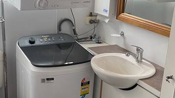 Uma lavanderia compacta com máquina de lavar de abertura frontal, pia e espelho acima.