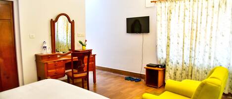 Quarto de hotel com cama, cômoda de madeira, cadeira, televisão e janela com cortinas.