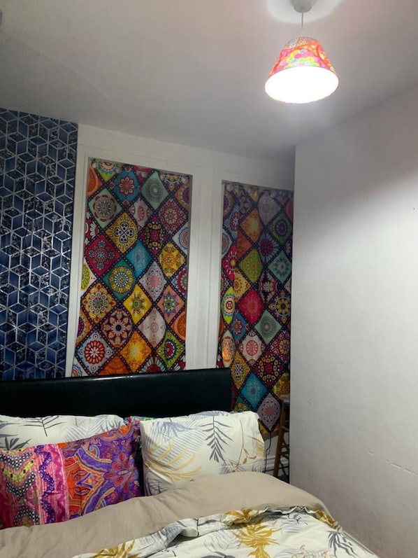 Quarto com cama, cortinas estampadas e luminária pendente.