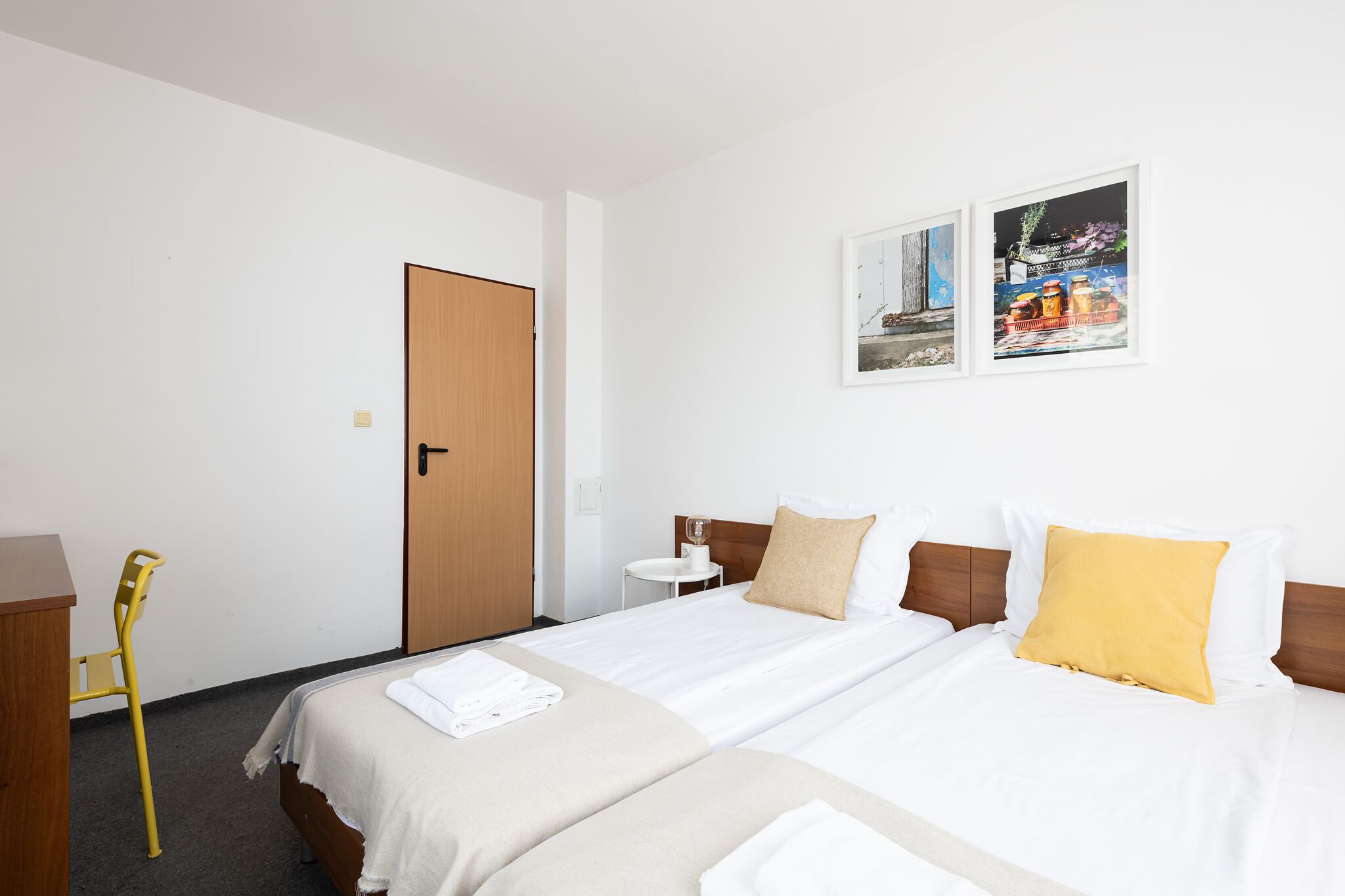 Quarto de hotel com cama de casal, mesa de cabeceira, uma cadeira e duas fotos emolduradas na parede.