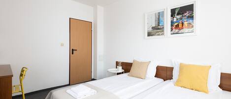 Quarto de hotel com cama de casal, mesa de cabeceira, uma cadeira e duas fotos emolduradas na parede.