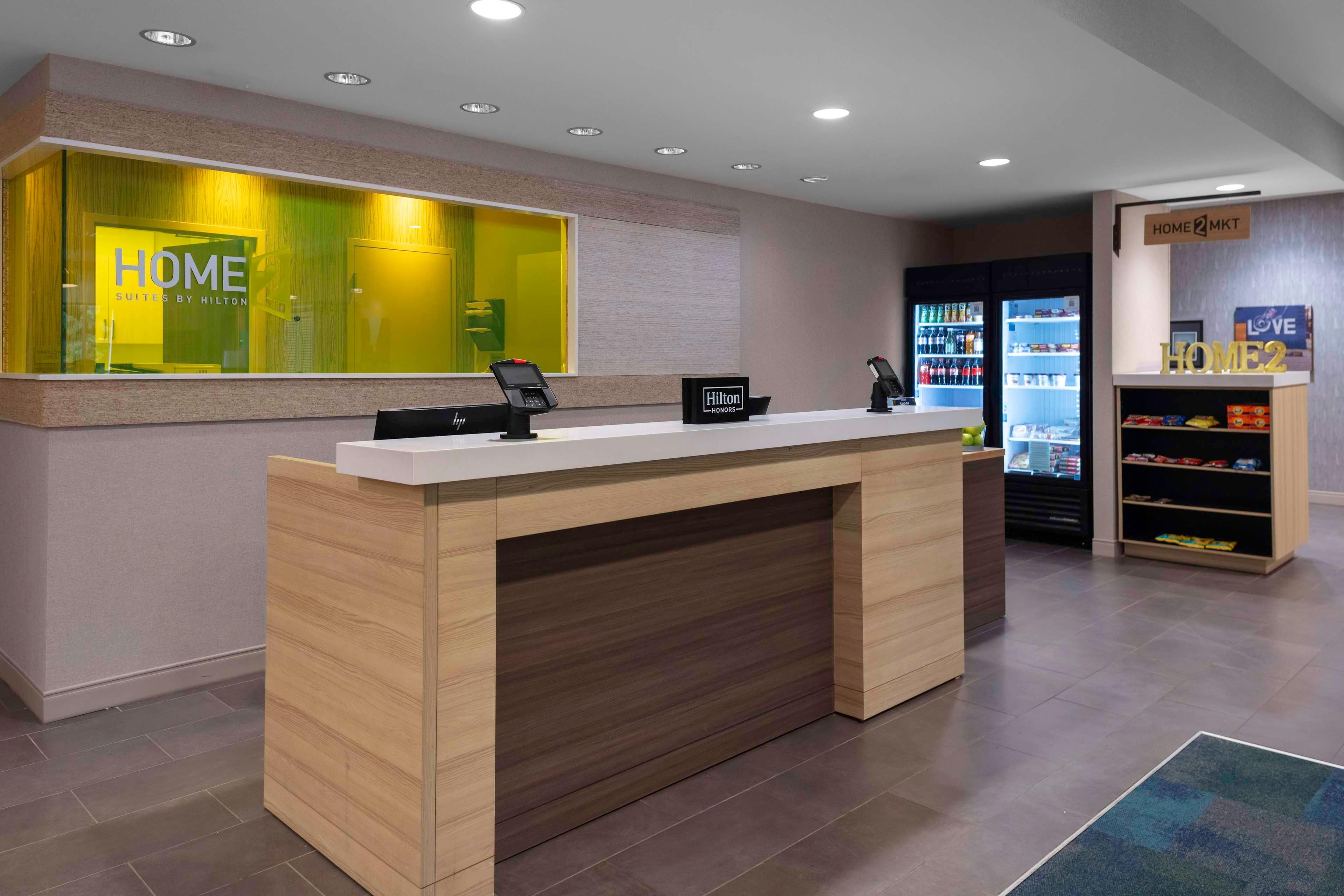 Uma receção de hotel moderna com um quiosque digital, um minibar e uma máquina de vendas automáticas.
