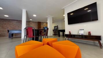 Um hall moderno com mesa de bilhar, cadeiras vermelhas, assentos laranja, televisão de tela plana e parede de tijolos.