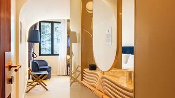Quarto de hotel moderno com parede curva, área de estar com uma cadeira azul, uma pequena mesa e um espelho grande.