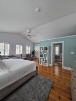 Quarto espaçoso com uma cama grande, um ventilador de teto e vista para o banheiro por uma porta aberta.
