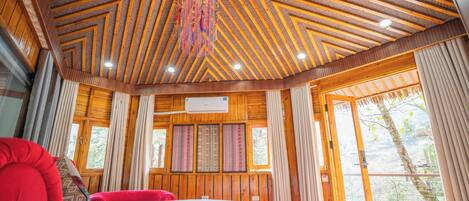 Uma cabana de madeira com uma cama, teto com padrão geométrico e grandes janelas.